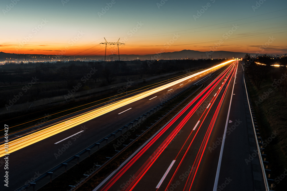 Cars light trails on a straight highway at sunset. Night traffic trails ...