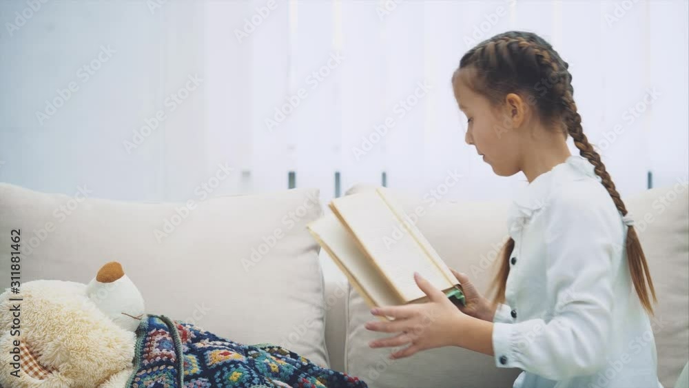Cute little girl reading fairy-tale for her teddy, petting it ...