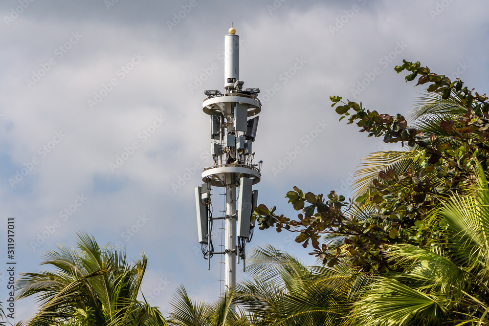 Gray metal cell tower carrying antennas of cellular networks on the blue sky with white clouds ...