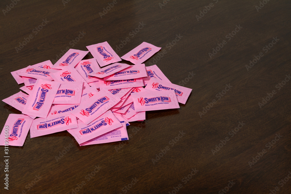 Pink packets of the artificial sweetener band of Sweet’n Low in a glass ...