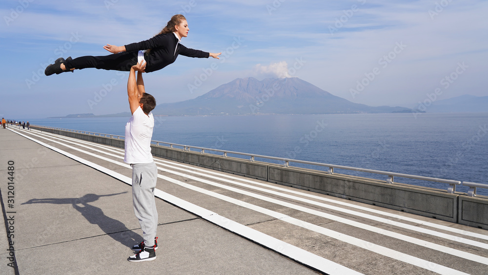 A young couple of acrobats on a background of a smoking volcano doing ...