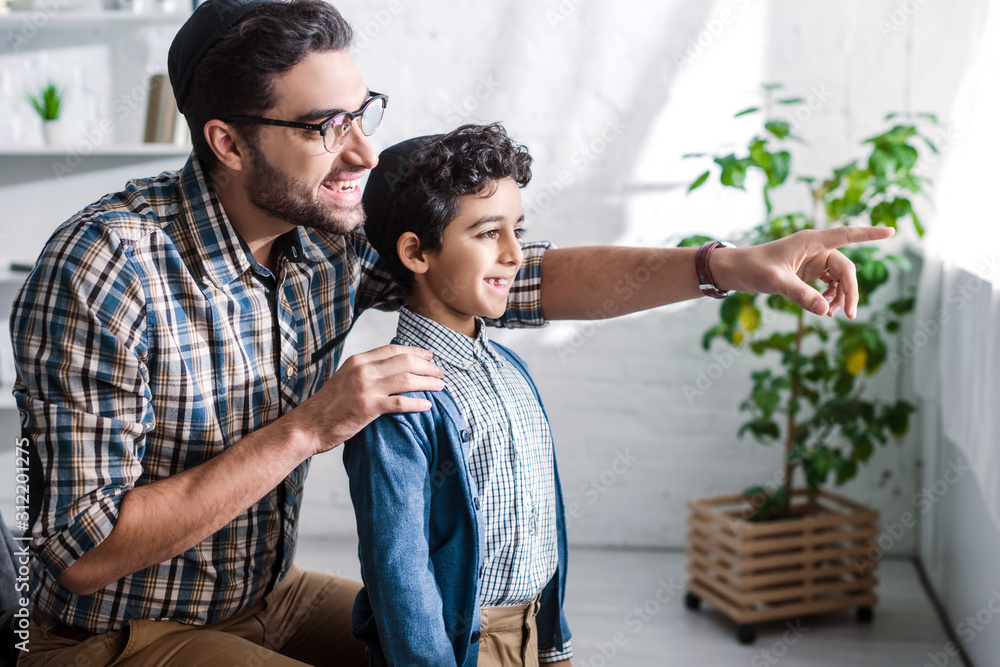 smiling jewish father pointing with finger and looking through window ...