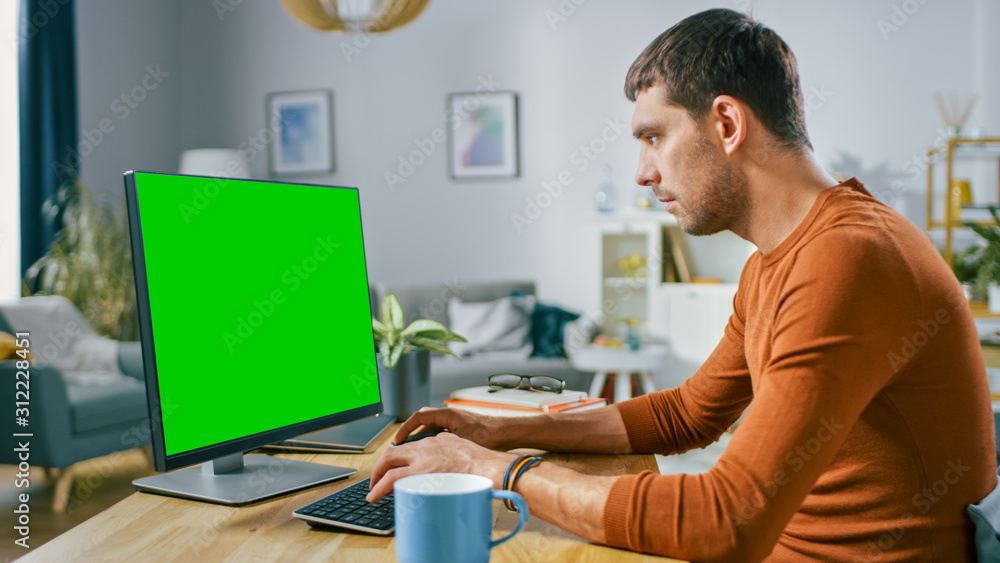 Handsome Smiling Man Sitting at His Desk at Home Uses Personal Computer ...