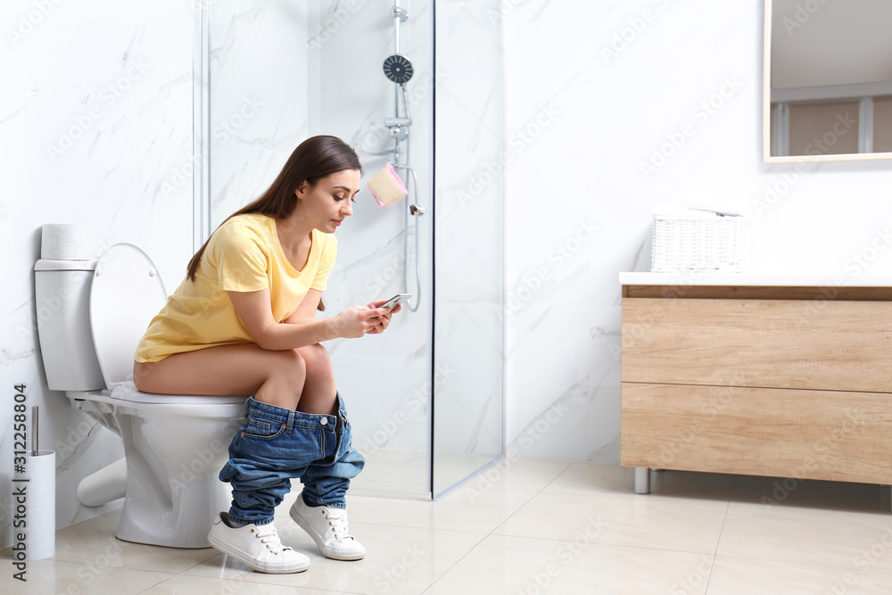 Woman with smartphone sitting on toilet bowl in bathroom Stock Photo ...