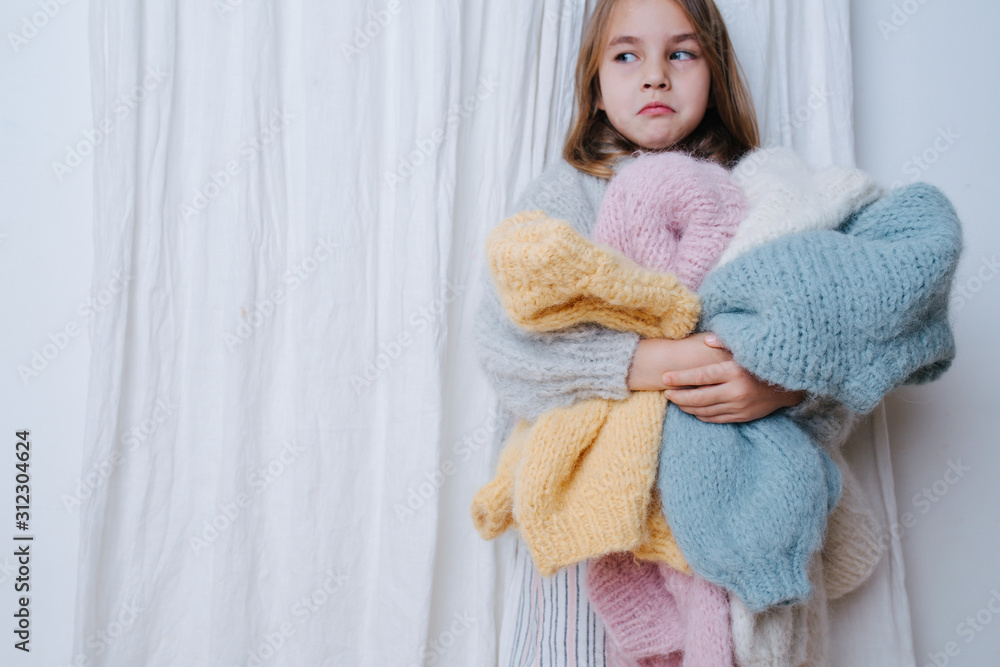 Sad unhappy little girl is hugging pile of soft fluffy multi-colored ...