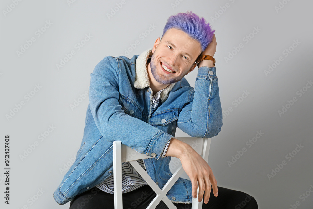 Portrait of stylish young man sitting on chair against light background ...