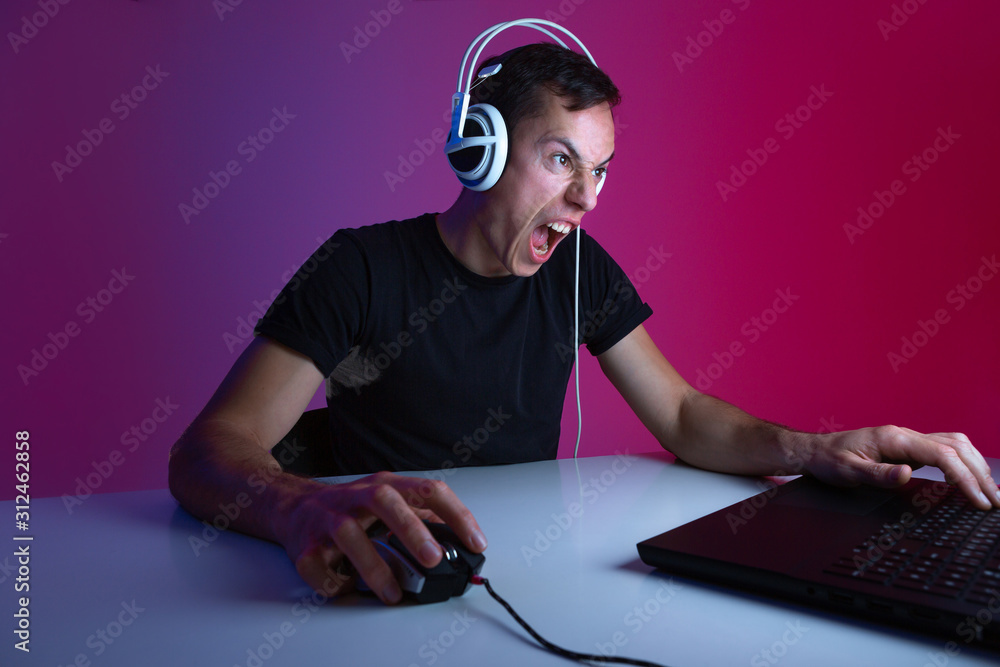 Angry gamer wearing headphones playing video games on computer in a ...