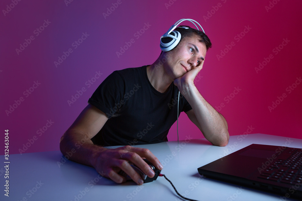 Tired gamer wearing headphones playing video games on computer in a ...