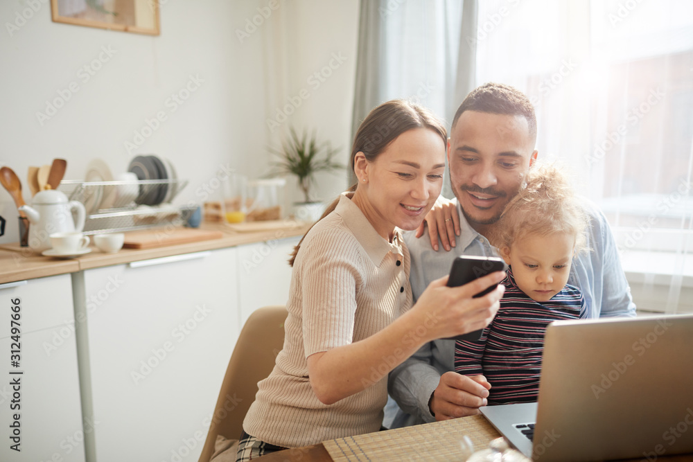 Warm-toned portrait of modern mixed race-family using computer devices ...