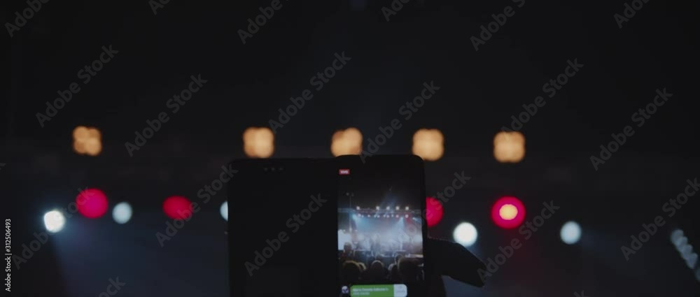 Person taking a picture during a concert, with floodlights flashing in ...
