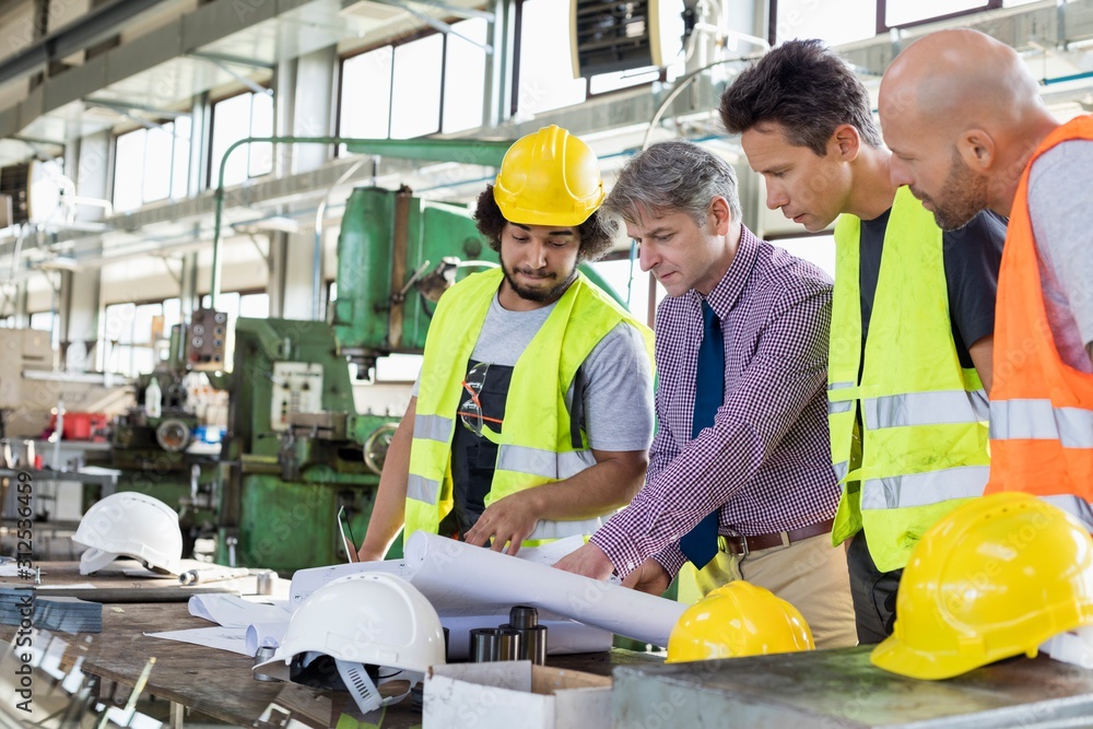 Male supervisor with workers discussing over blueprints in industry ...
