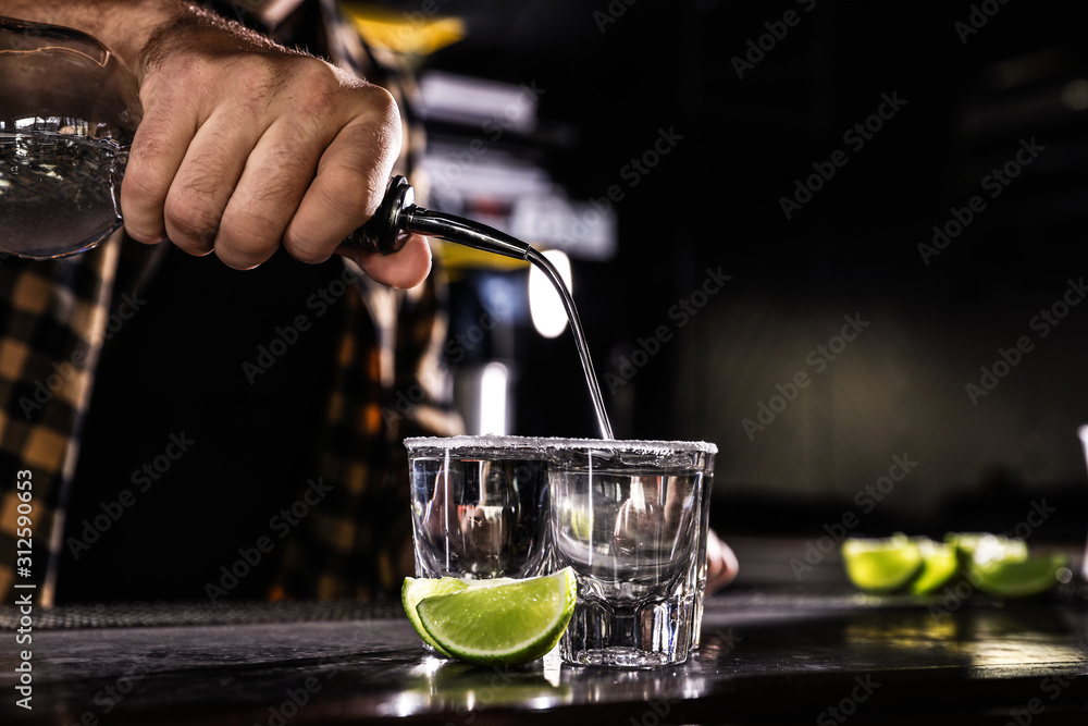 Bartender pouring Mexican Tequila into shot glasses at bar counter ...