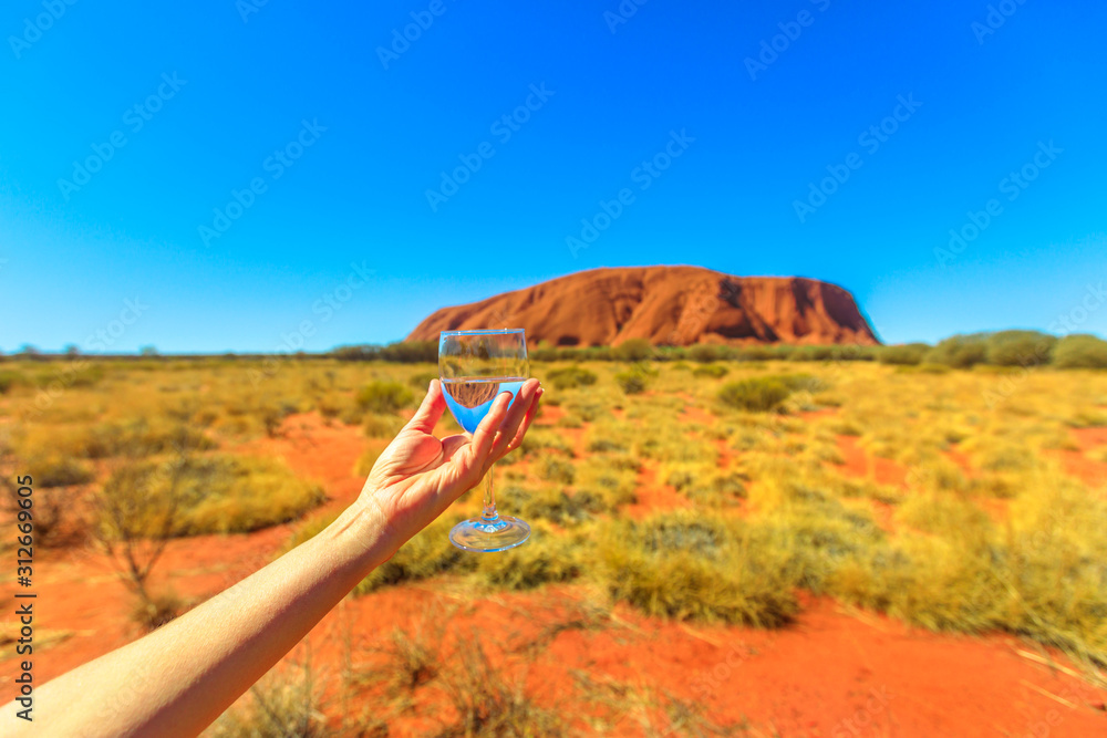 Woman's hand holding a glass goblet that reflecting Ayers Rock in Uluru ...