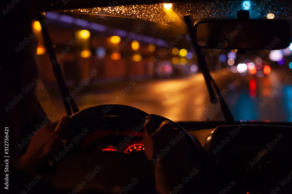 driving car in night city, hands of driver on steering wheel and street ...