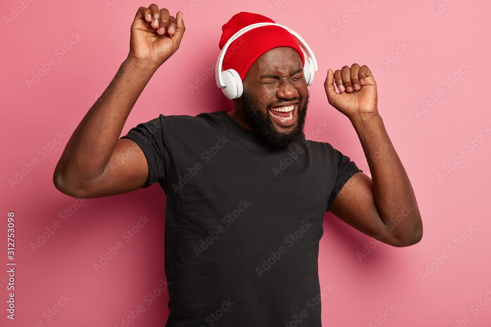 Feeling happy and relaxed. Joyful dark skinned man enjoys funny melody ...