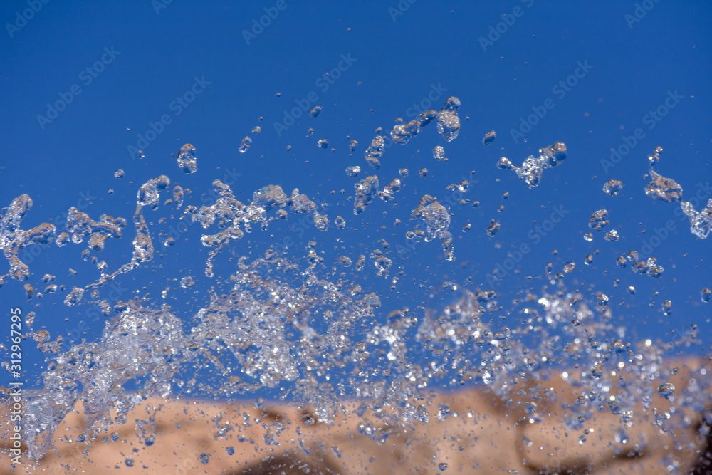 Water droplets spraying from a fountain in abstract design on blue sky ...