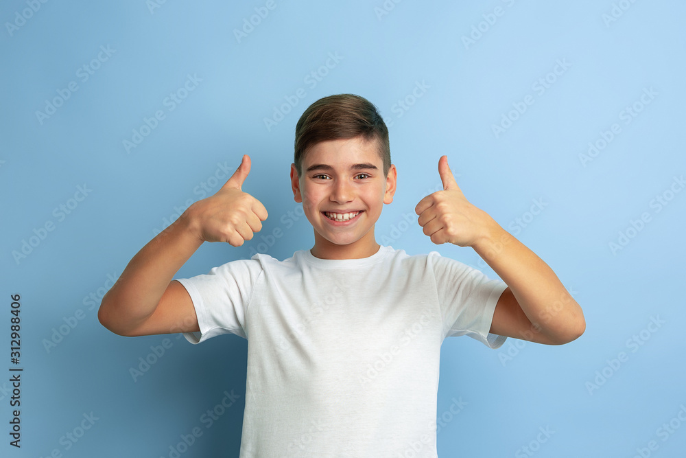 Showing thumbs up, smiling. Caucasian boy portrait isolated on blue ...