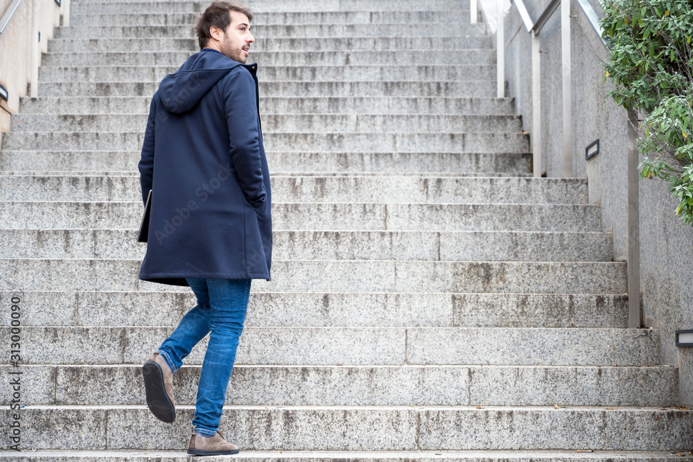 Horizontal portrait of young attractive man standing on steps looking ...