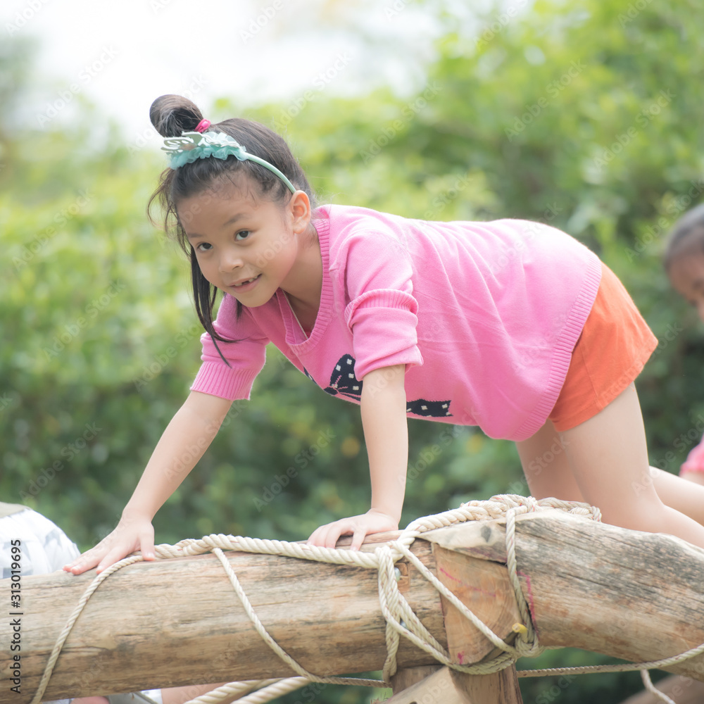 Little Girl with climbing gear climbing rope trail in an adventure park ...