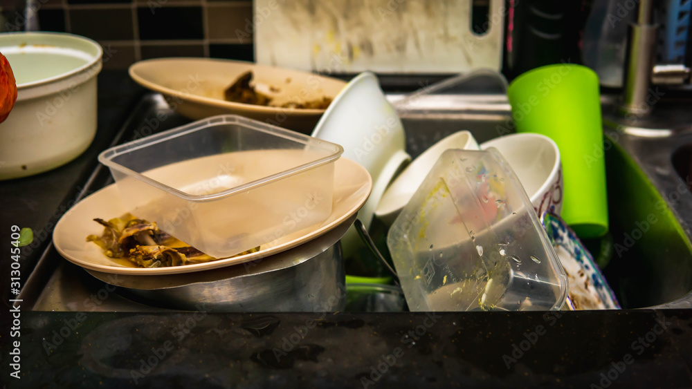 Dirty dishes, utensil, plastic container and food waste piled in a ...