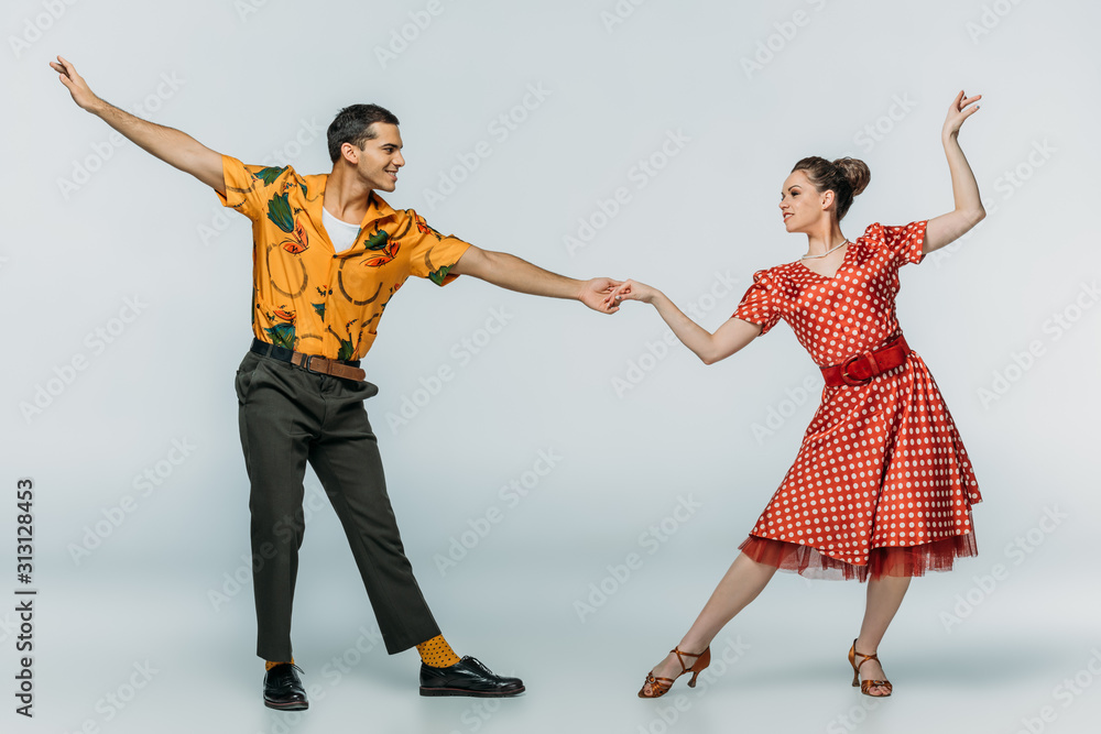 elegant dancers holding hands while dancing boogie-woogie on grey ...