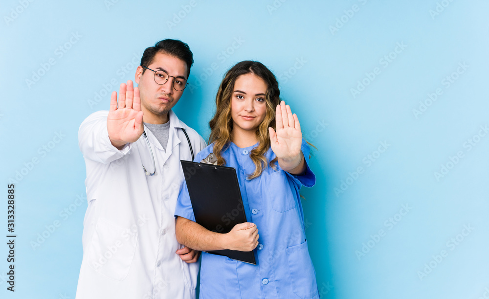 Young doctor couple posing in a blue background isolated standing with ...