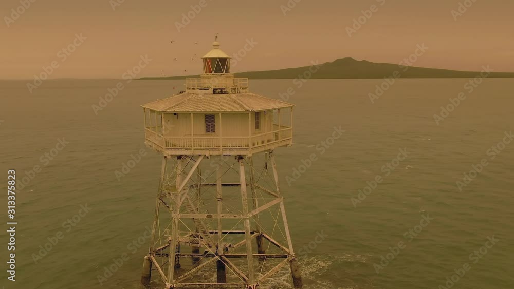Aerial: Rangitoto Island, Bean Rock Lighthouse and orange skies created ...