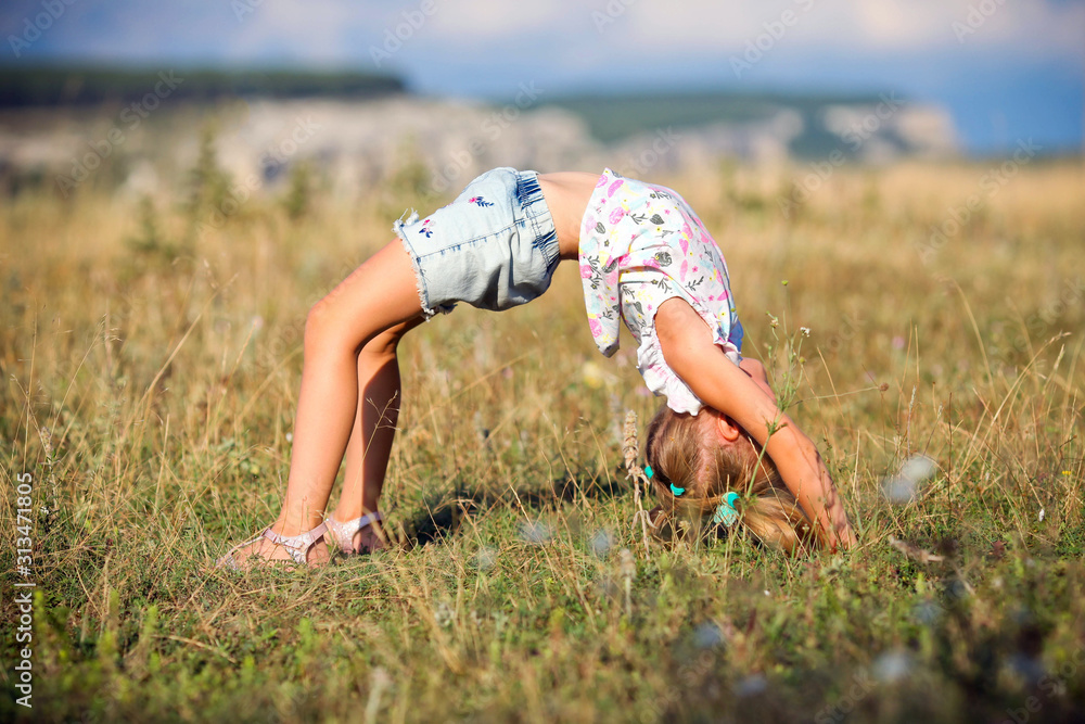 A little girl makes a bridge, bending her back in nature. A flexible ...