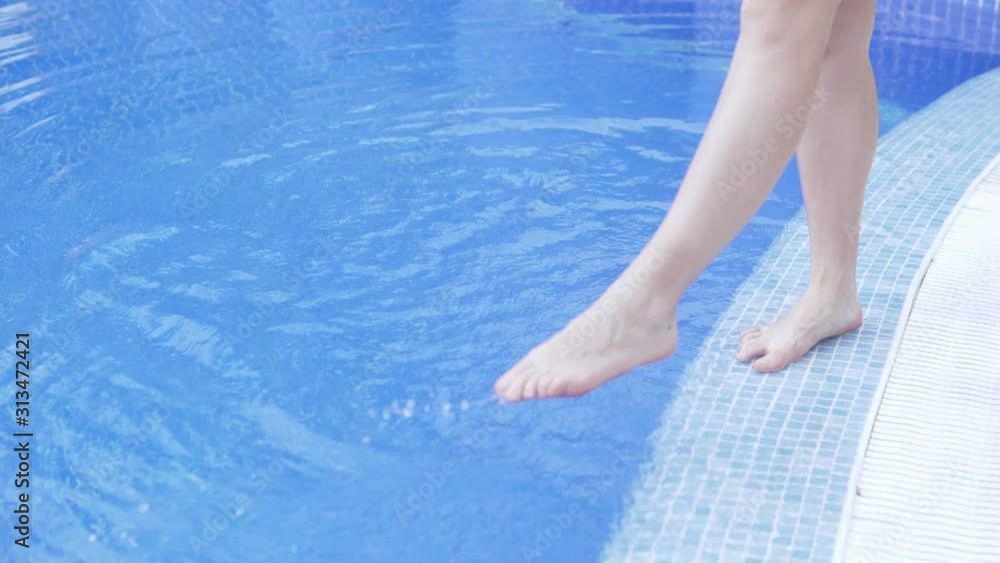 Women's feet by the pool. Woman wets feet in pool, checks water ...