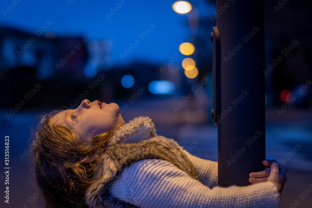 cute little girl is embracing a streetlight pylon and she is looking up ...