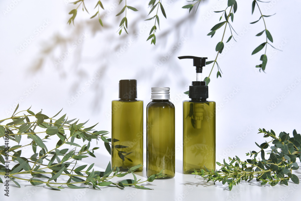 Cosmetic bottle containers packaging with green herbal leaves in shadow ...