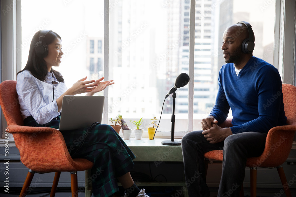 Smiling female journalist interviewing businessman while sitting on ...