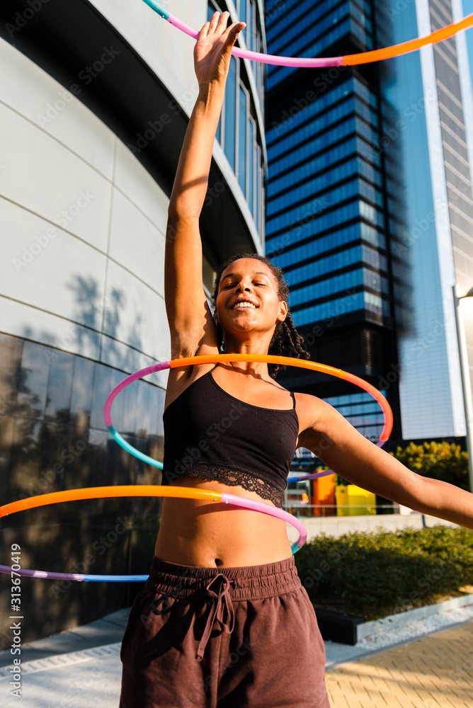 Generation Z woman performing Hula Hoop dance with rings in downtown ...