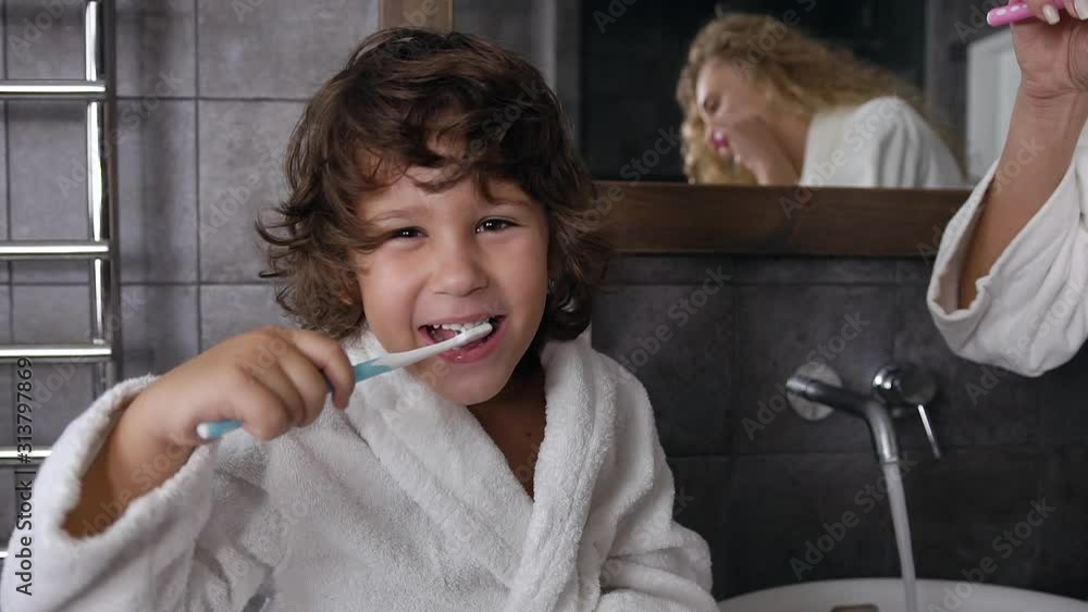 Cheerful little boy with curly hair in a white coat is brushing his ...