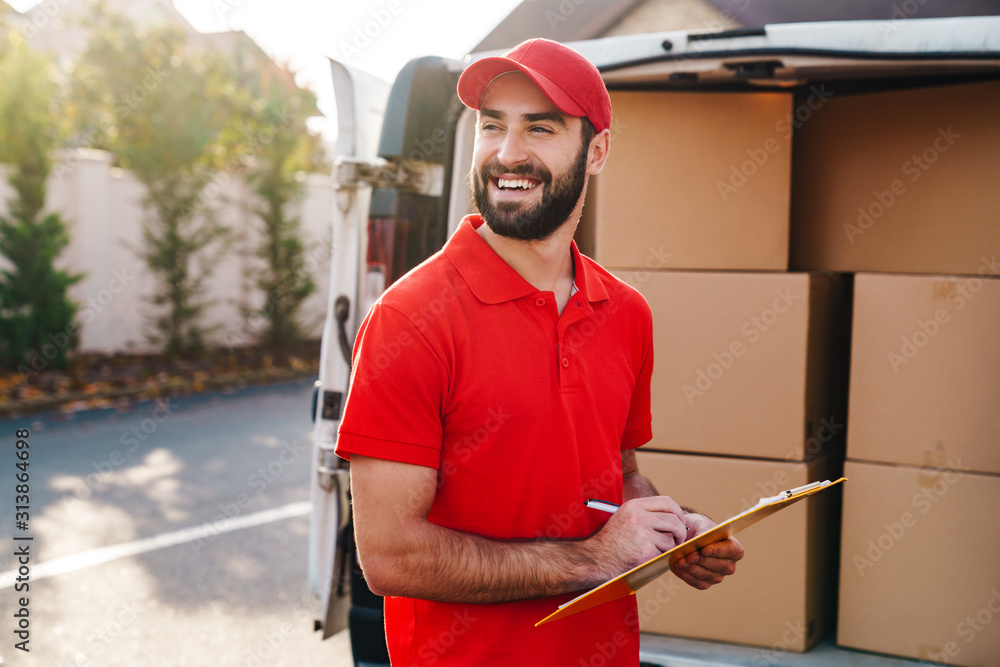 Image of smiling delivery man holding clipboard and writing Stock Photo ...