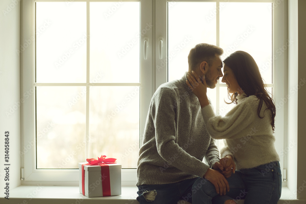 Rear view of a young couple sitting on a window sill by the window ...