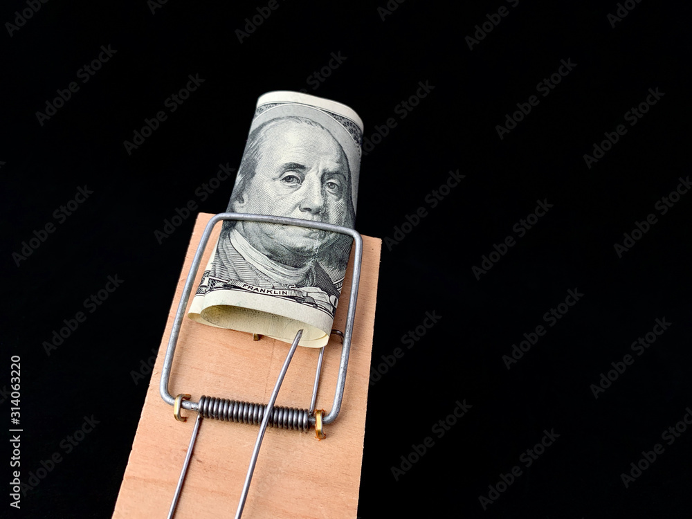 Dollars in a mousetrap on a black background. Wooden trap with bait and ...