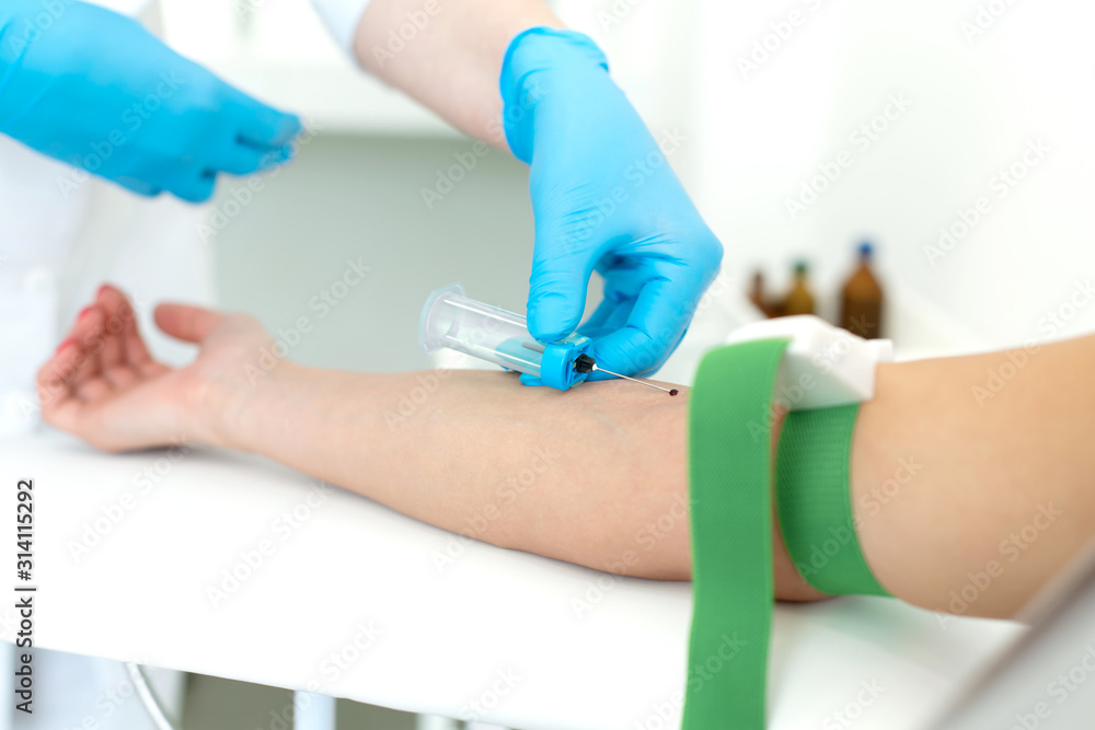 a gloved nurse inserts a needle into a vein on the patient arm and ...