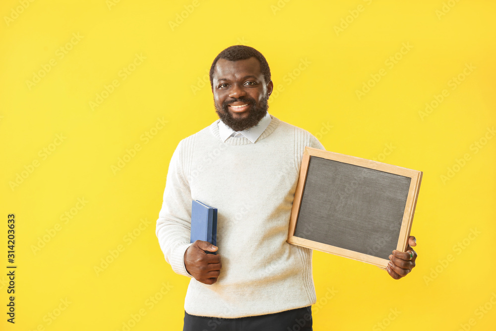 African-American teacher with chalkboard and book on color background ...