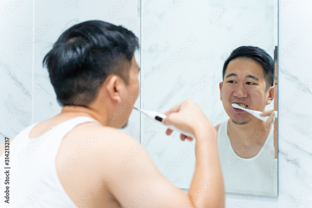 Back view of Asian guy in white shirt brushing teeth with an electric ...