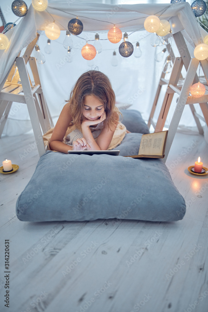 Little 10 year old girl using tablet under her home-made tent inside ...