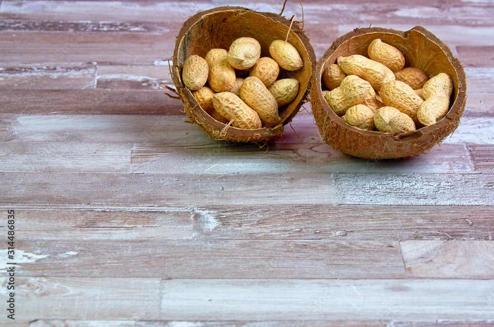 Peanuts lies in a coconut shell on a wooden table with place for text ...