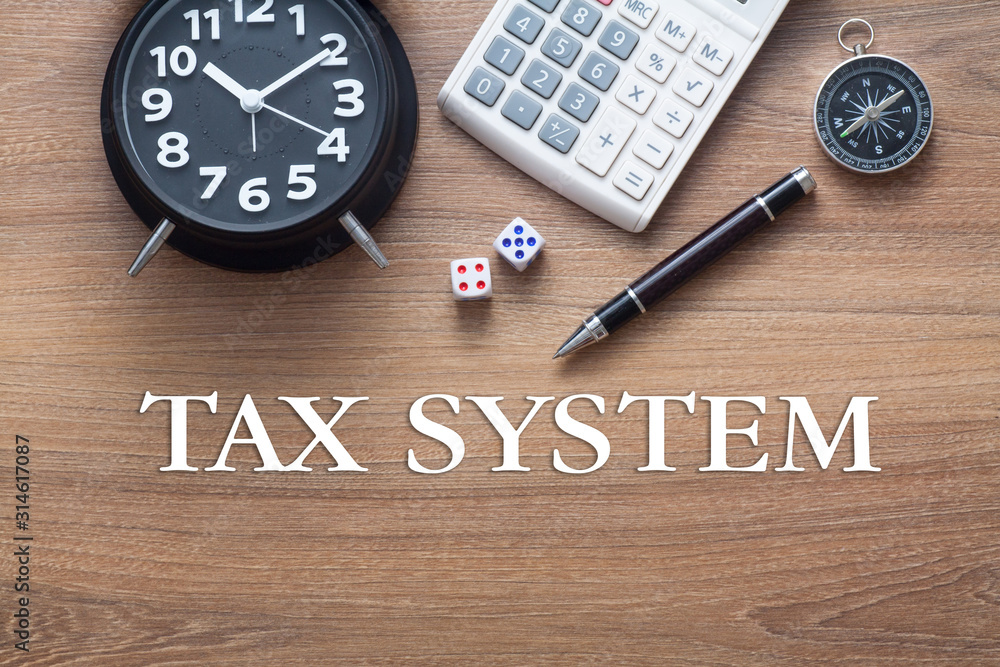 Tax System words written on wooden table with clock,dice,calculator pen ...