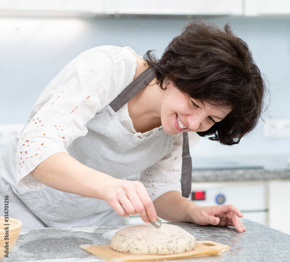 Smiling woman making patterns on raw bread using a knife or blade to ...