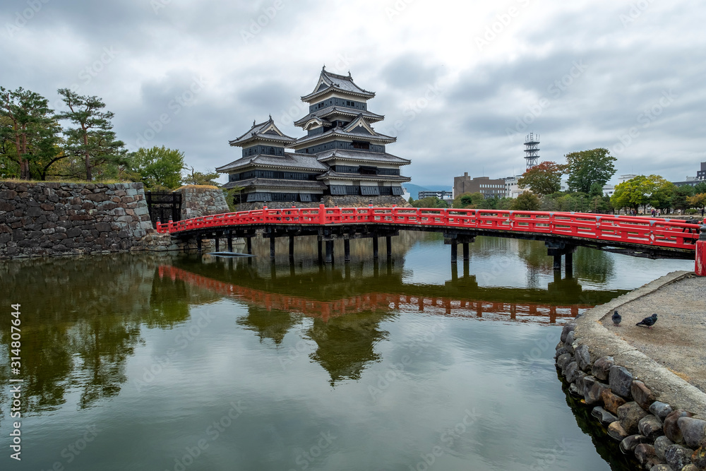 Matsumoto castle with red bridge and it’s reflection over water against ...