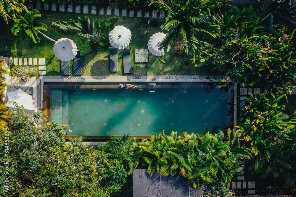 A young girl sits near the infinity pool with azure water. Villa in the ...