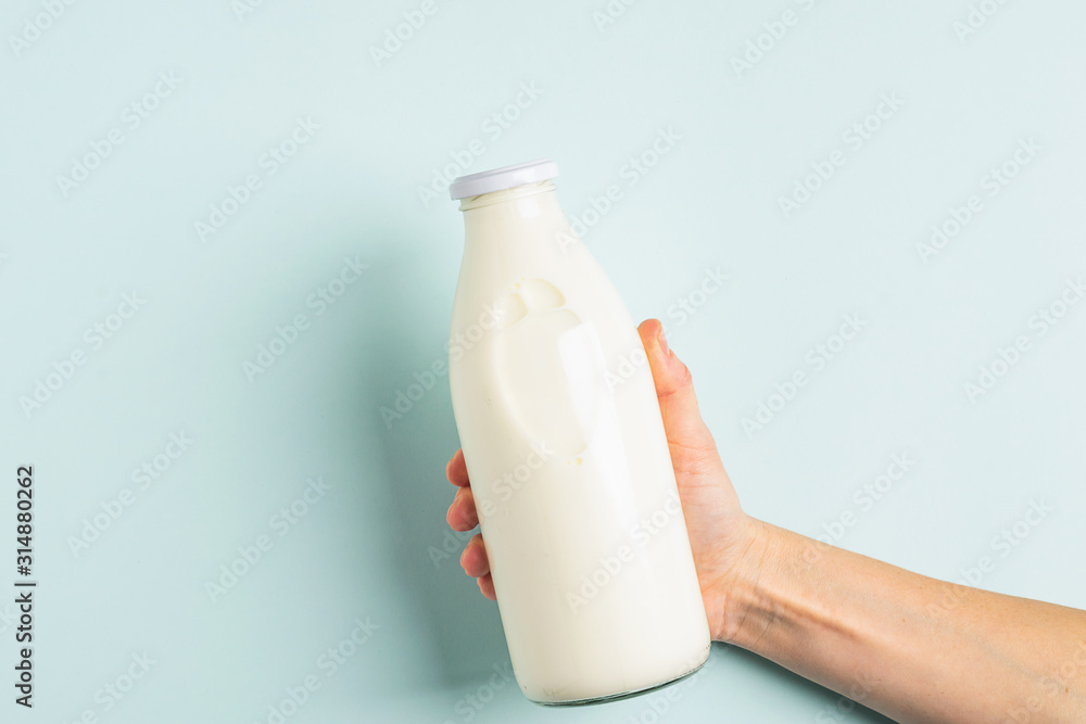 Female hand holds milk or white milk drink in a glass bottle on white ...