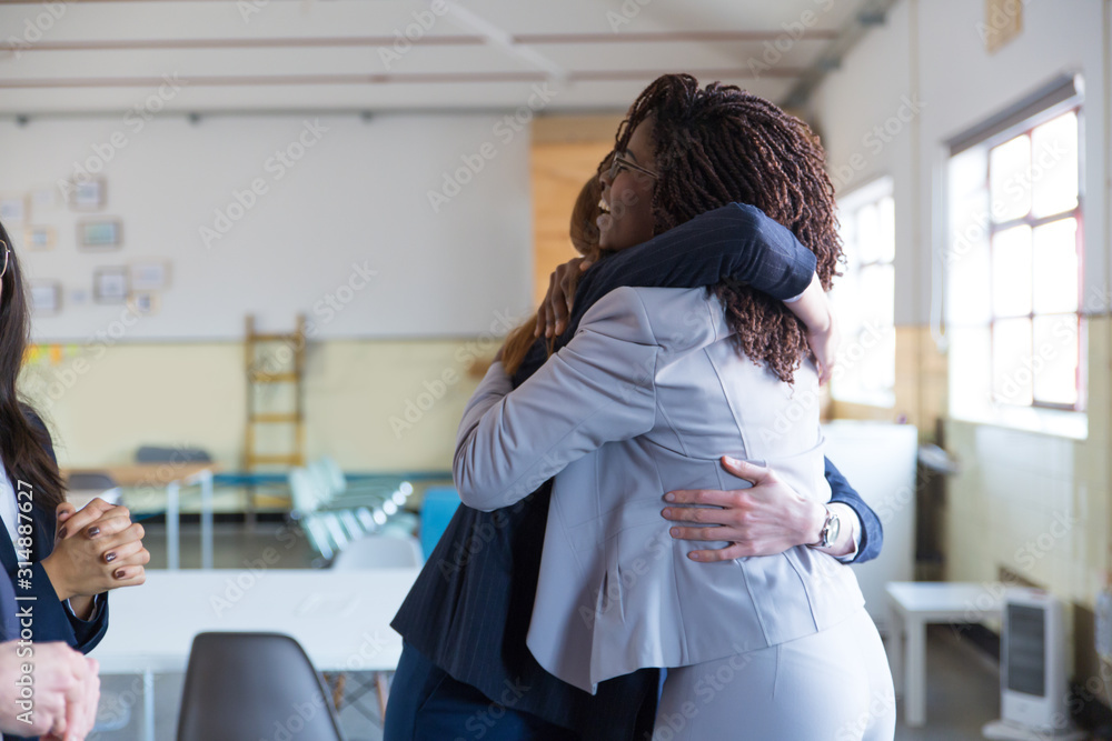 Excited businesswomen hugging in office. Group of happy multiethnic ...