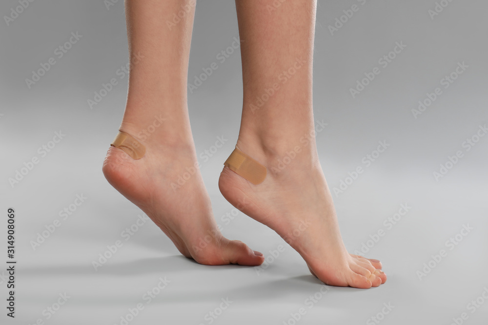 Girl showing feet with sticking plasters on light grey background ...