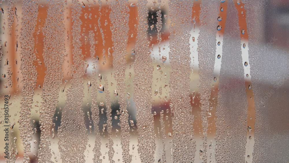 Misted glass of window with water drops falling down and blurred ...